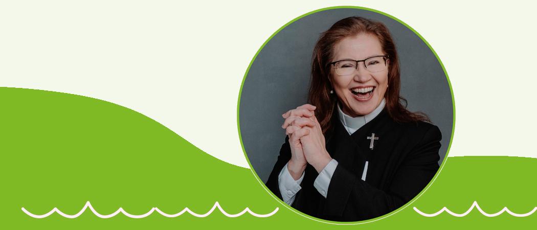 Kannelmäen seurakunnan kirkkoherra hymyilee, kädet olkapään kohdalla ...